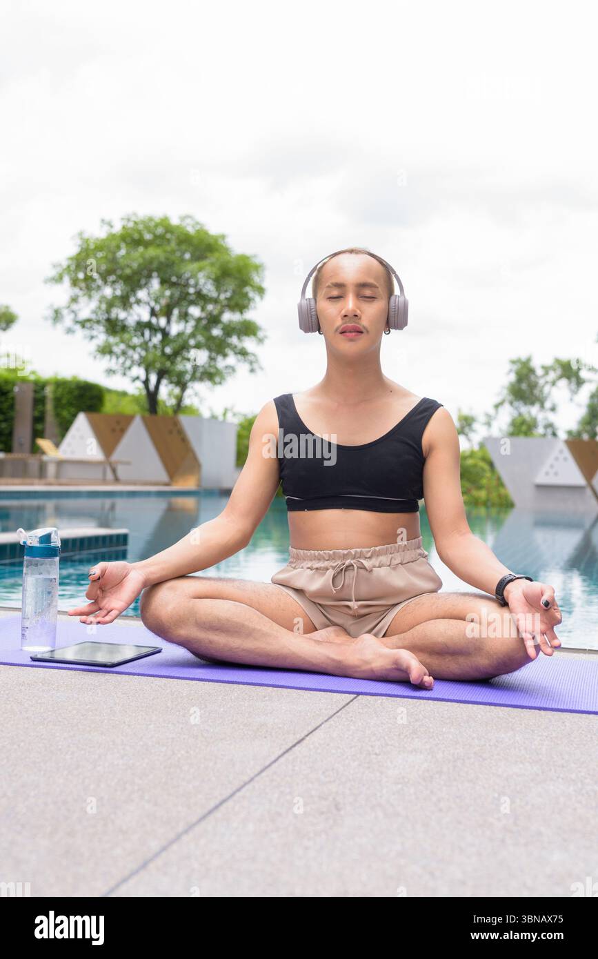 Non-binary Asian person exercising in poolside doing yoga and wearing ...