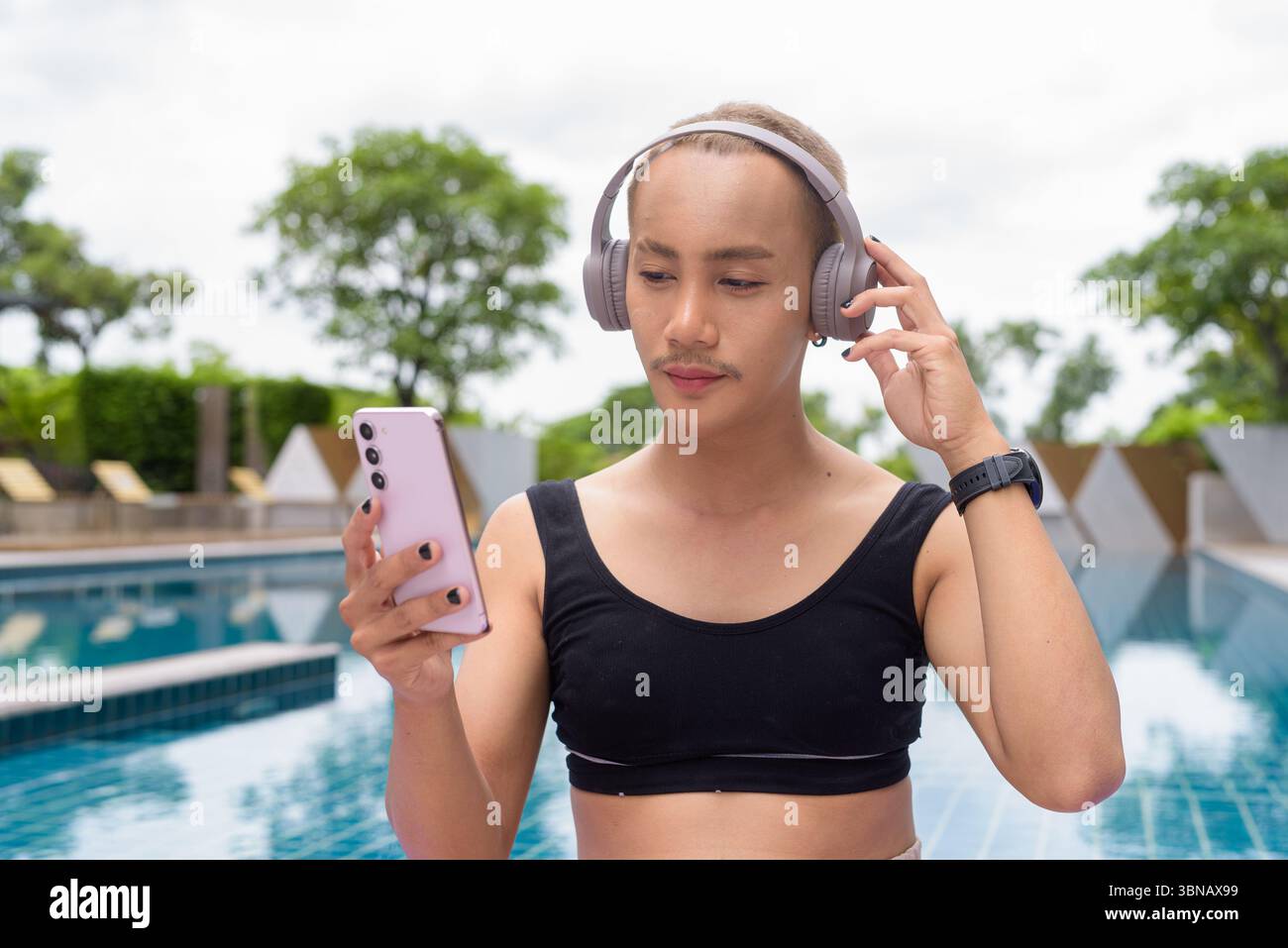 Non-binary Asian person exercising in poolside doing yoga and wearing ...