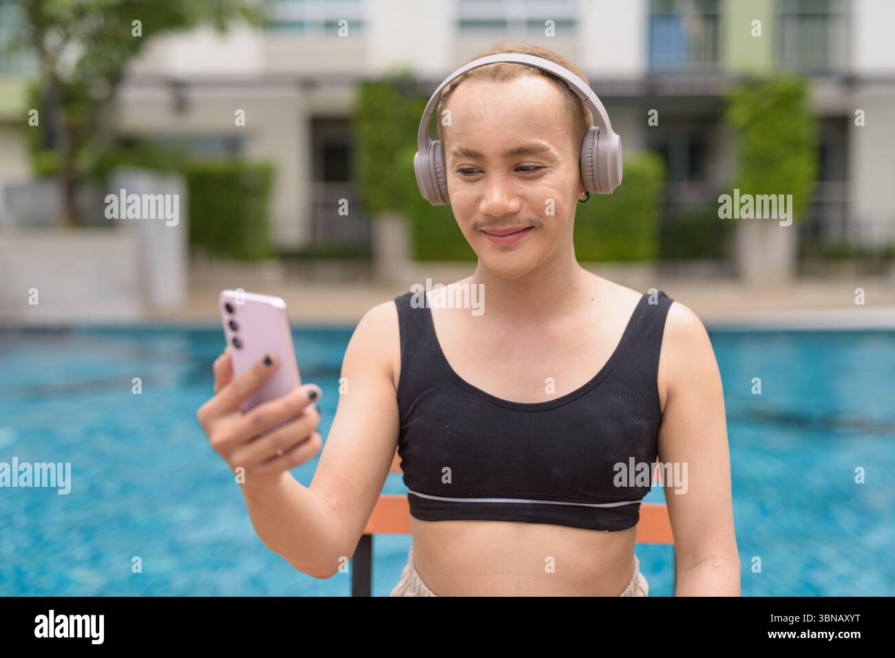 Non-binary Asian person relaxing in poolside during summer wearing ...