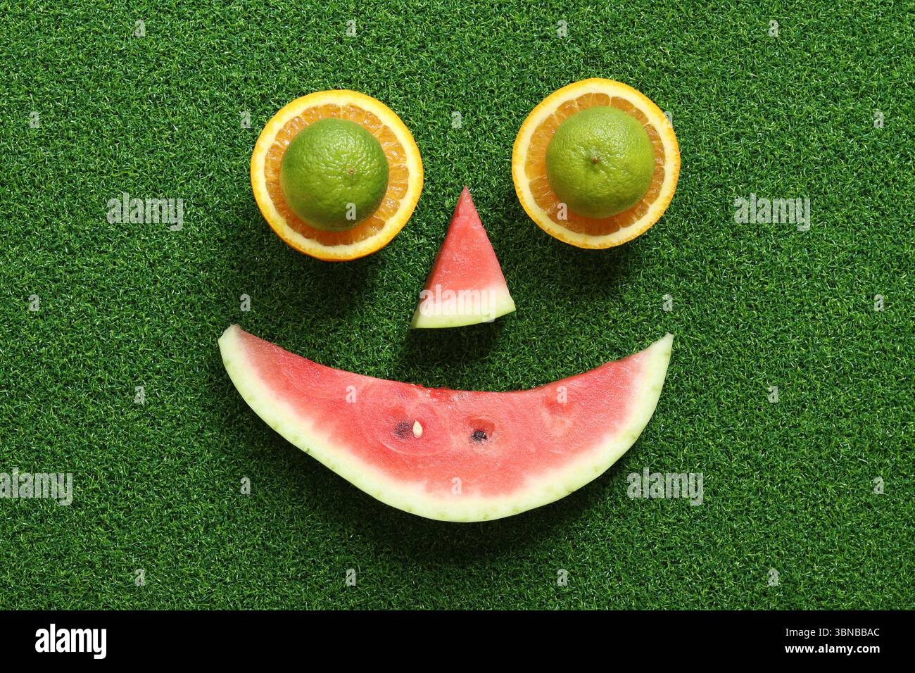 Fruit face. Orange and lime halves, watermelon slice on green grass ...