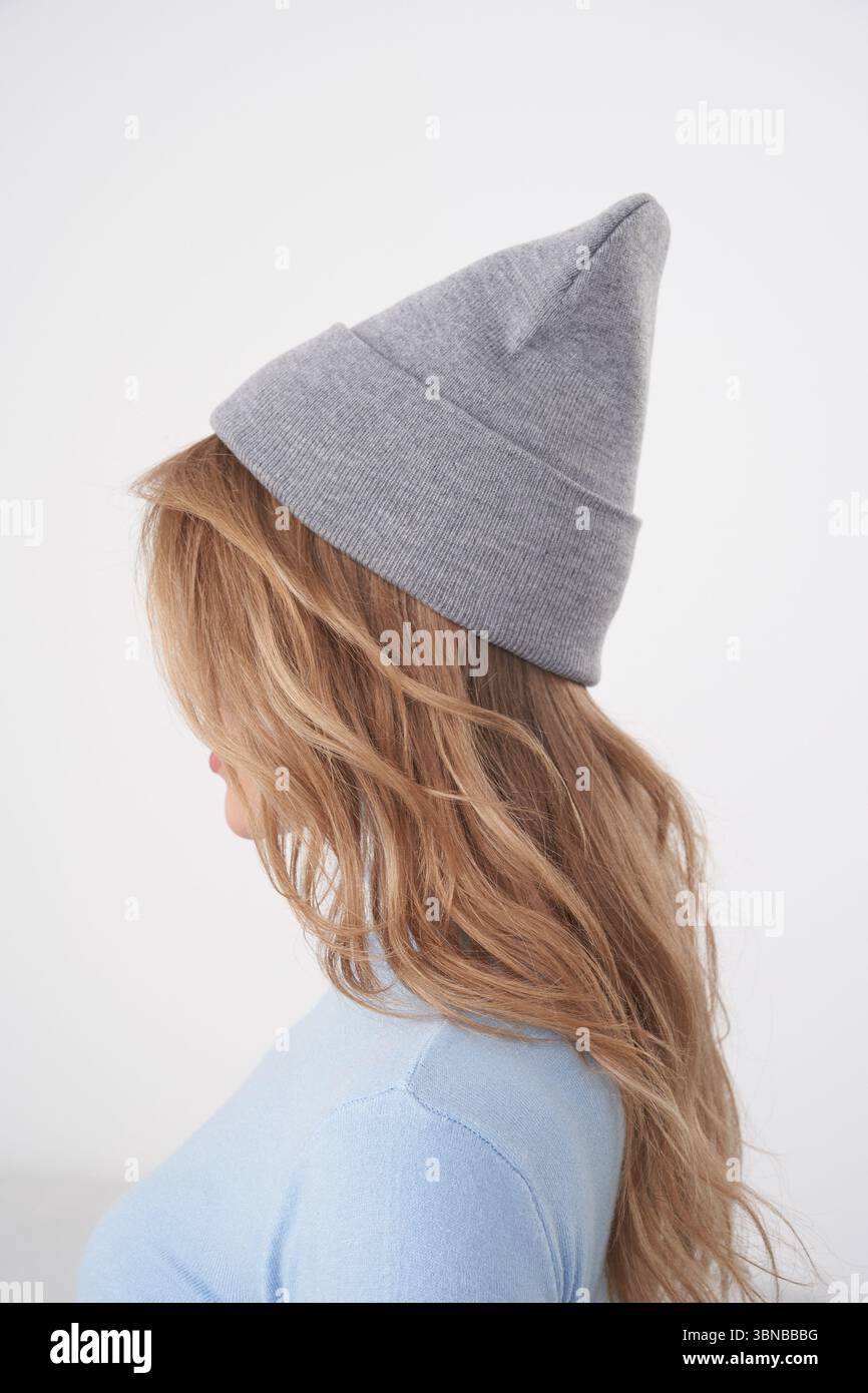 Side view of individual with long, wavy hair, wearing a grey knit ...