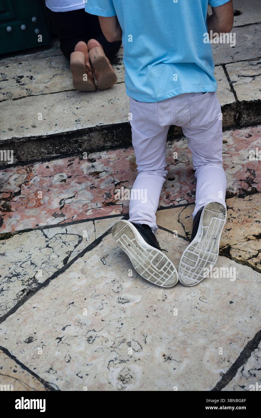 Body part view of people kneeling praying at the door of a church. Legs ...