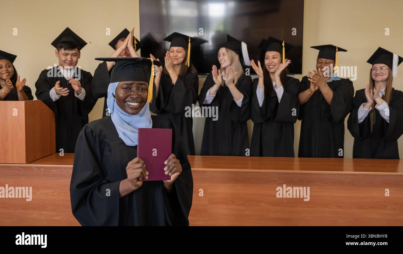 Happy African woman in hijab receiving diploma and classmates ...