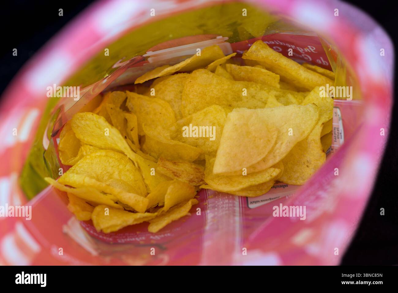 Top-down view of golden potato chips inside an open snack bag. The ...