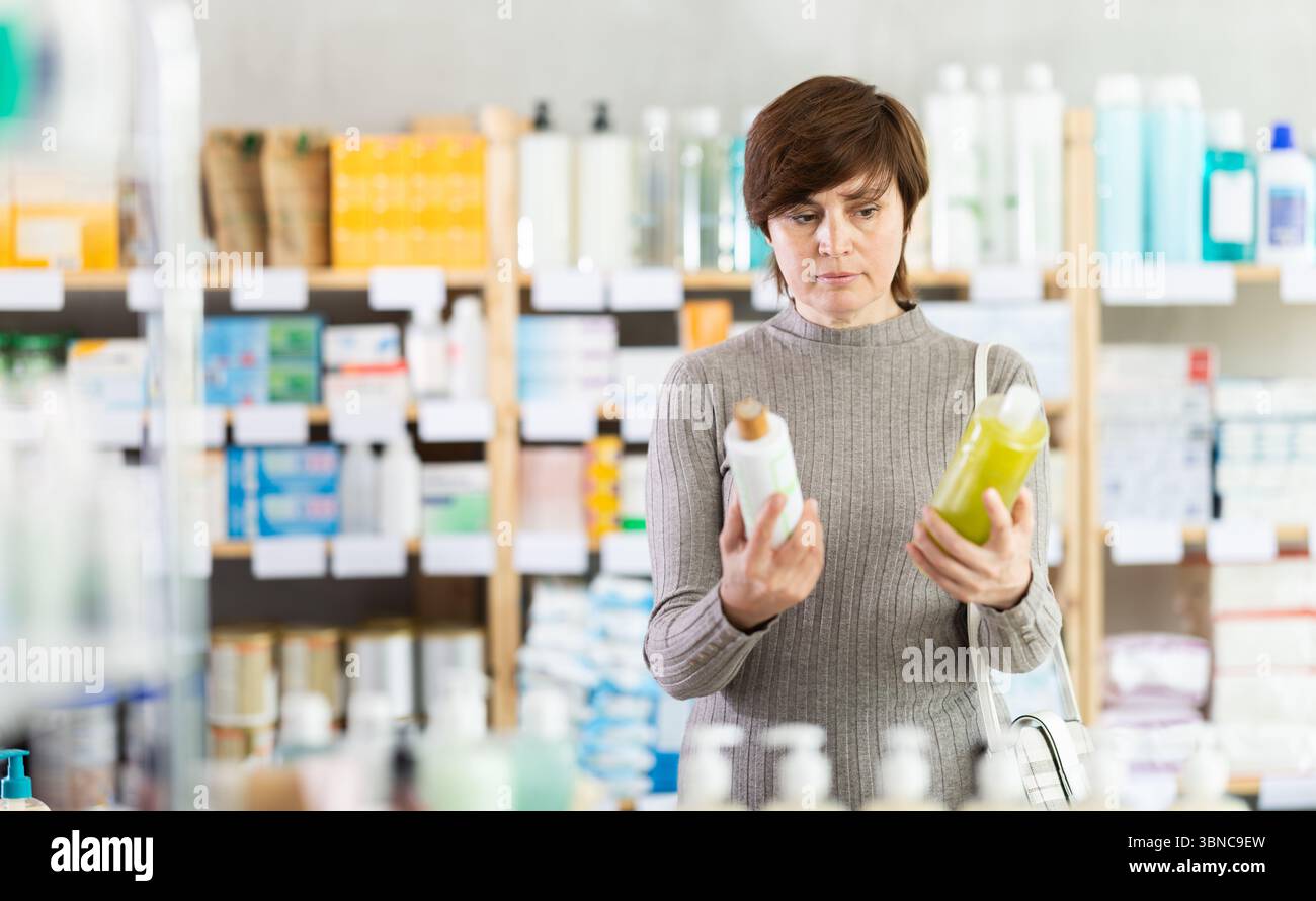 Female shopper in autumn clothes chooses medicated shampoo at pharmacy ...