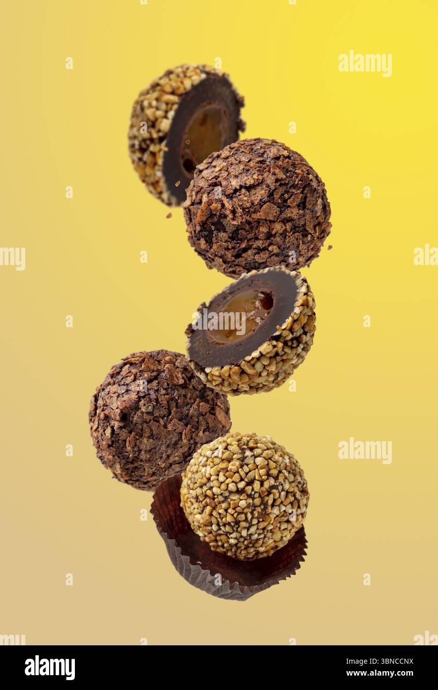 Round candies in chocolate and nut crumbs fly on a yellow background ...