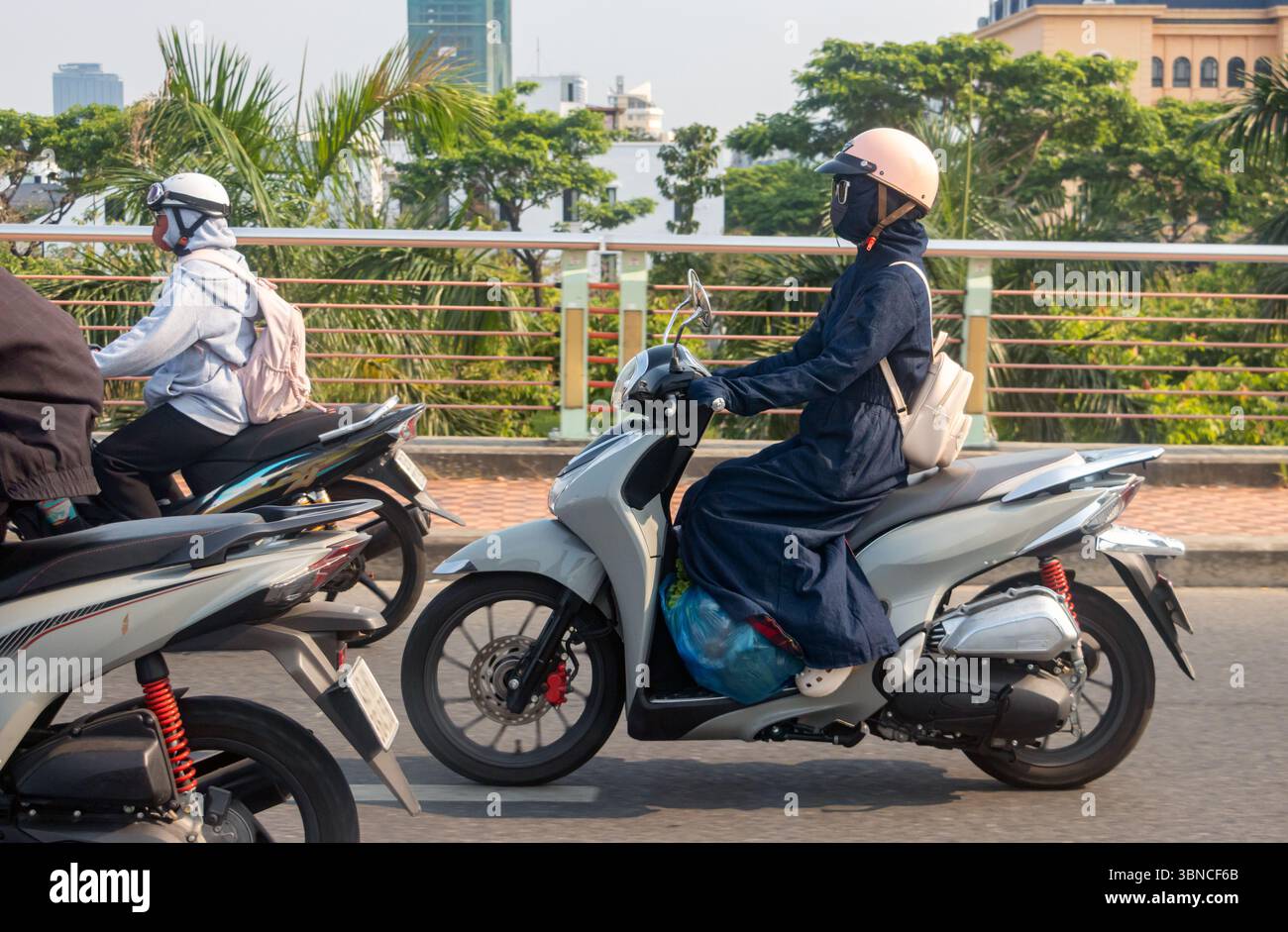 A woman fully covered in hooded clothing rides a motorbike, Da Nang ...