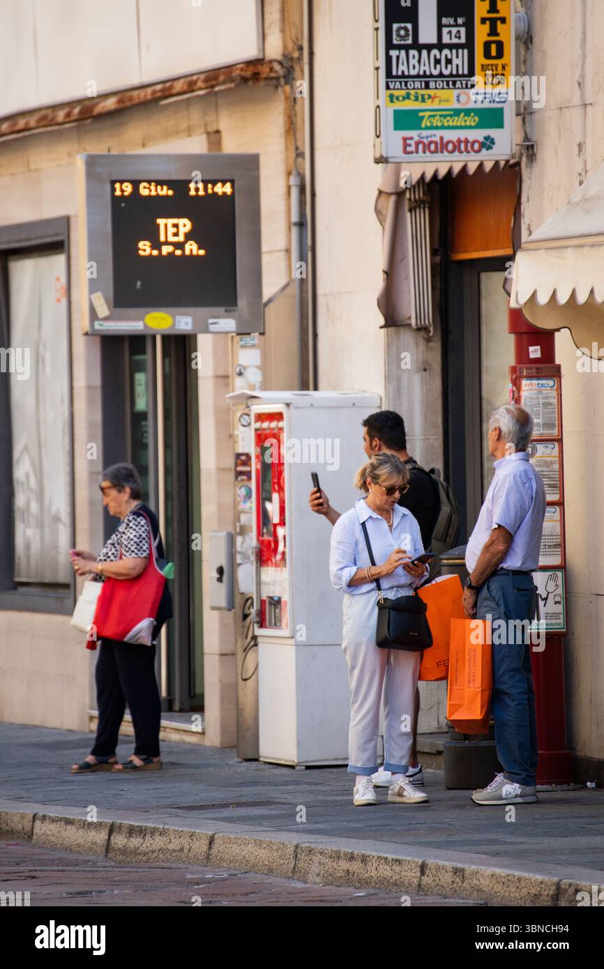People wait at an Italian bus stop urban setting with digital screen ...