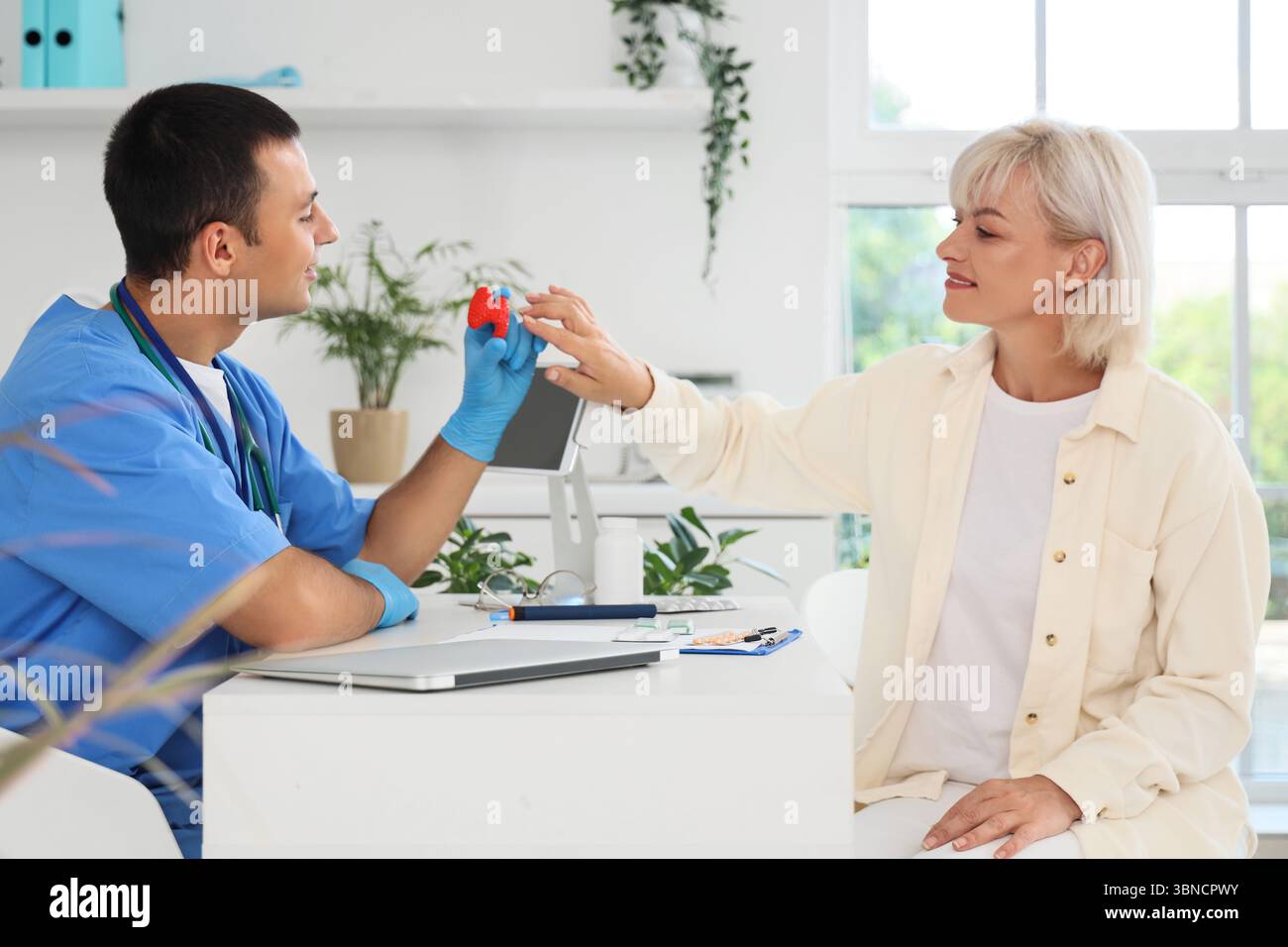 Male endocrinologist showing thyroid gland model to female patient at ...
