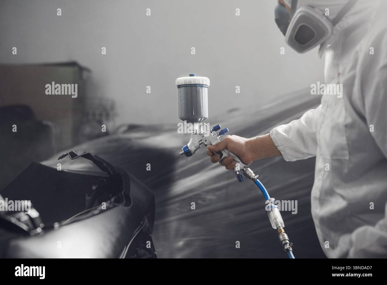 Auto mechanic worker spraying part of car to black color using spray ...