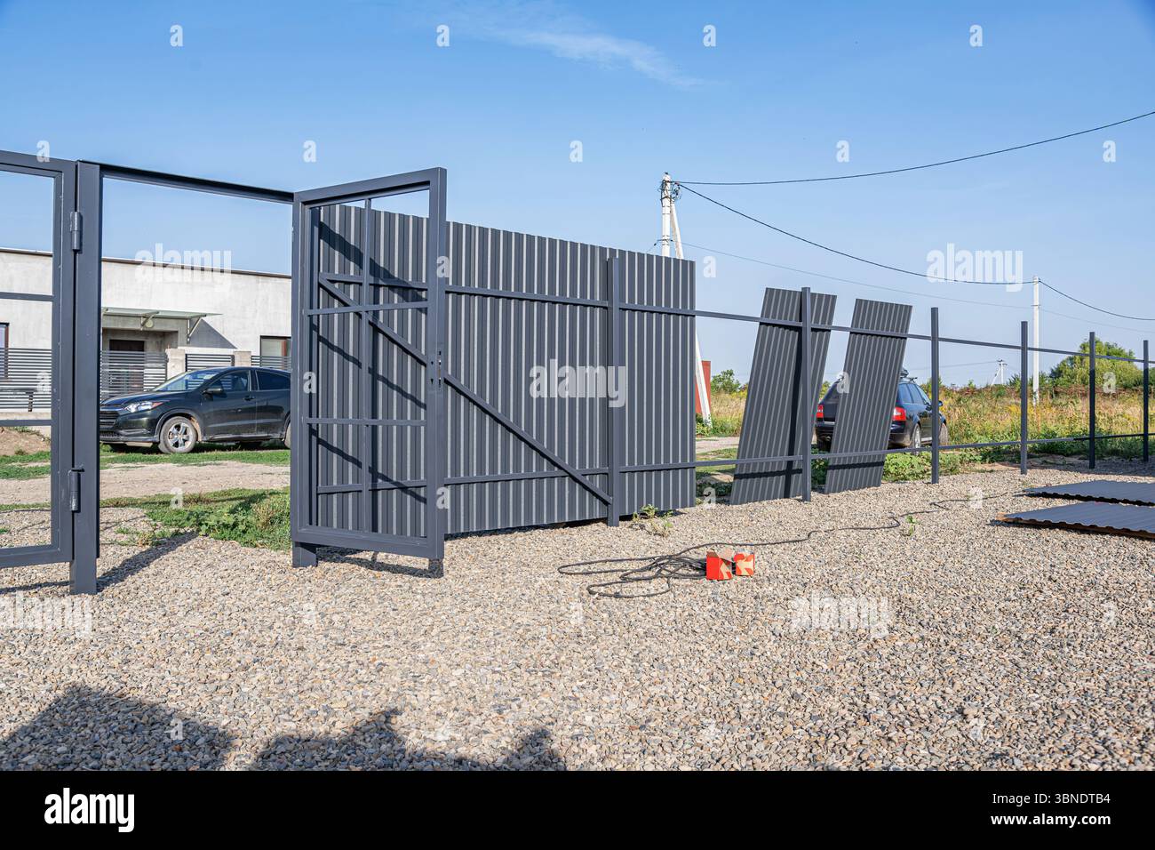 A partially installed corrugated metal fence with an open gate Stock ...