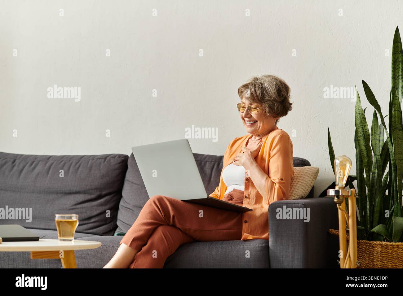A mature woman sits comfortably in her cozy attire with a laptop on her ...