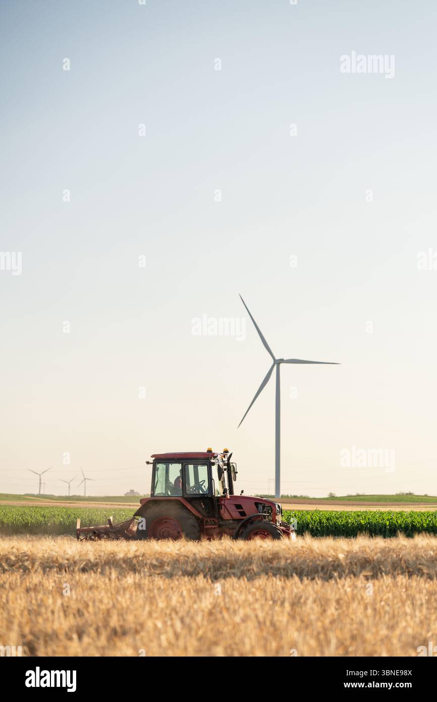 Agricultural tractor is working on the field with wind turbines Stock ...