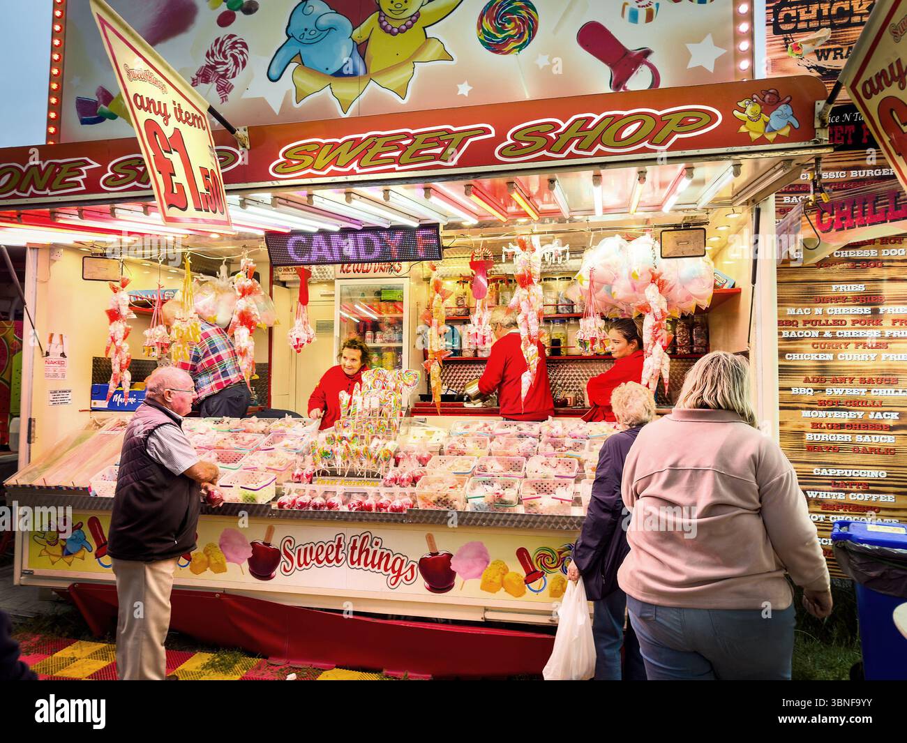 Customers browse an illuminated candy stall at a fair, featuring ...
