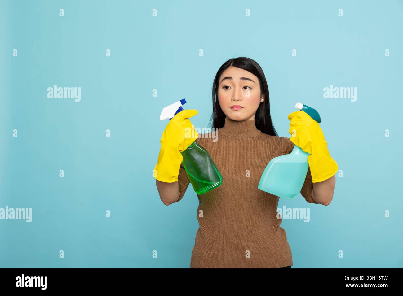 Pretty female janitor with yellow rubber gloves, holding two spray ...