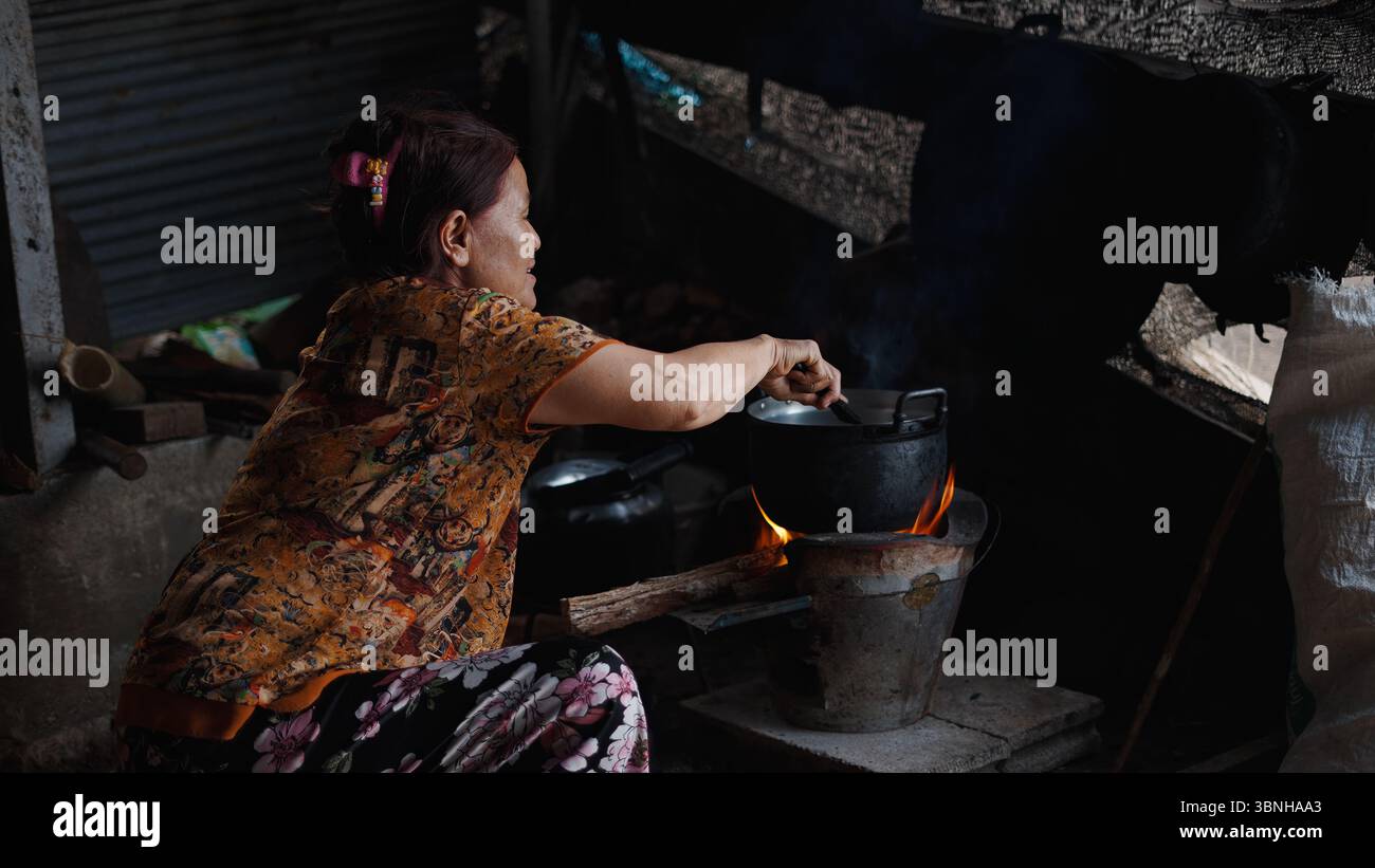 Southeast asian woman preparing a meal in a basic kitchen, using a wood ...