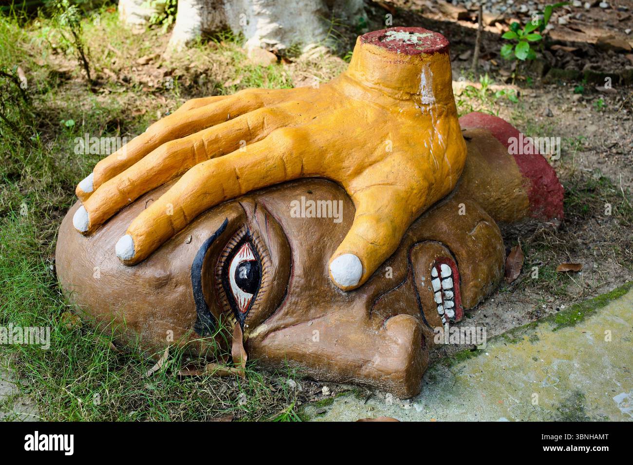 Sculpture of a large yellow hand pressing down on a head, in the grounds of Natore Rajbari ...