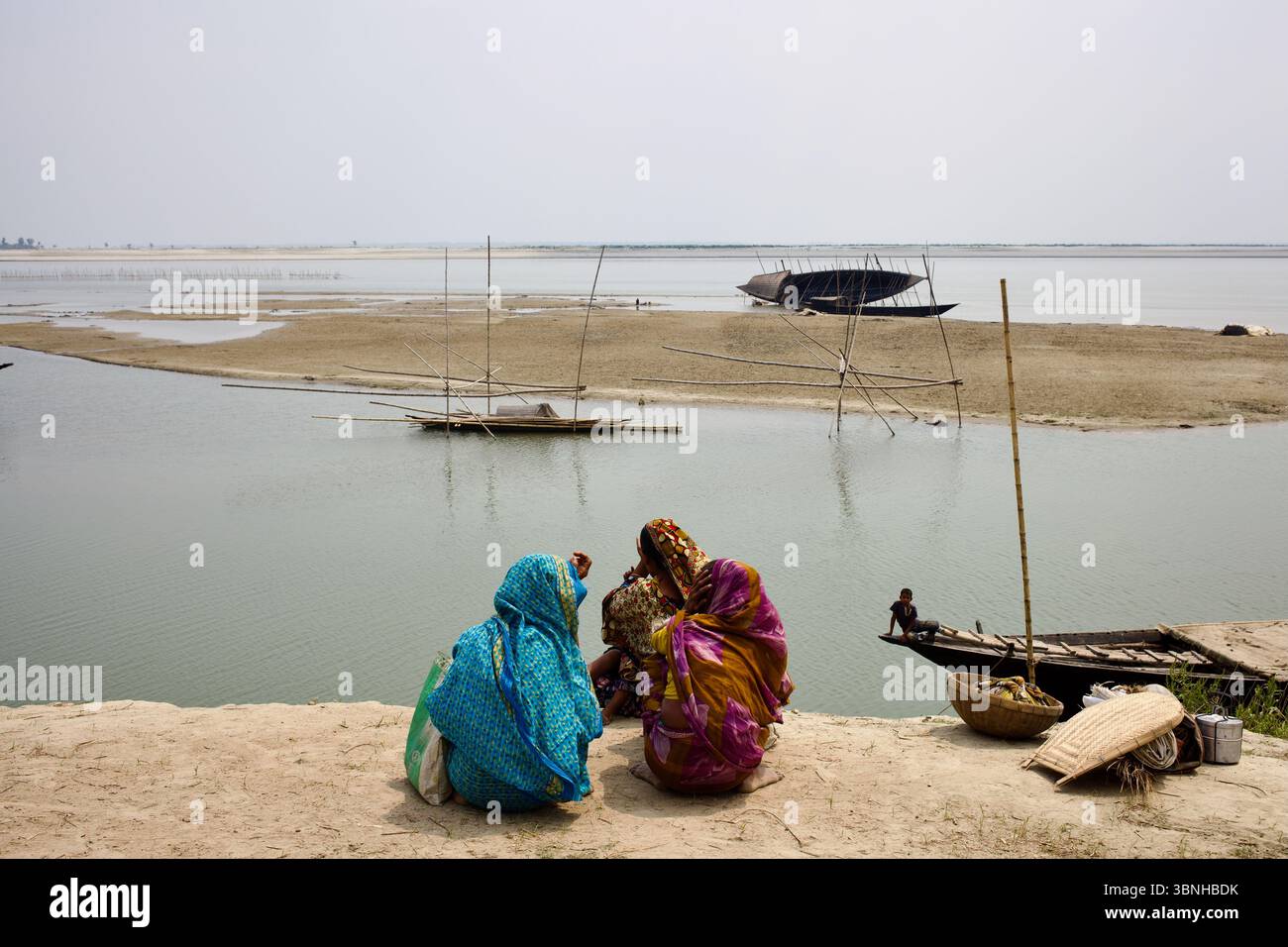 Women sit by the Brahmaputra River in Chilmari, Kurigram, while bamboo ...