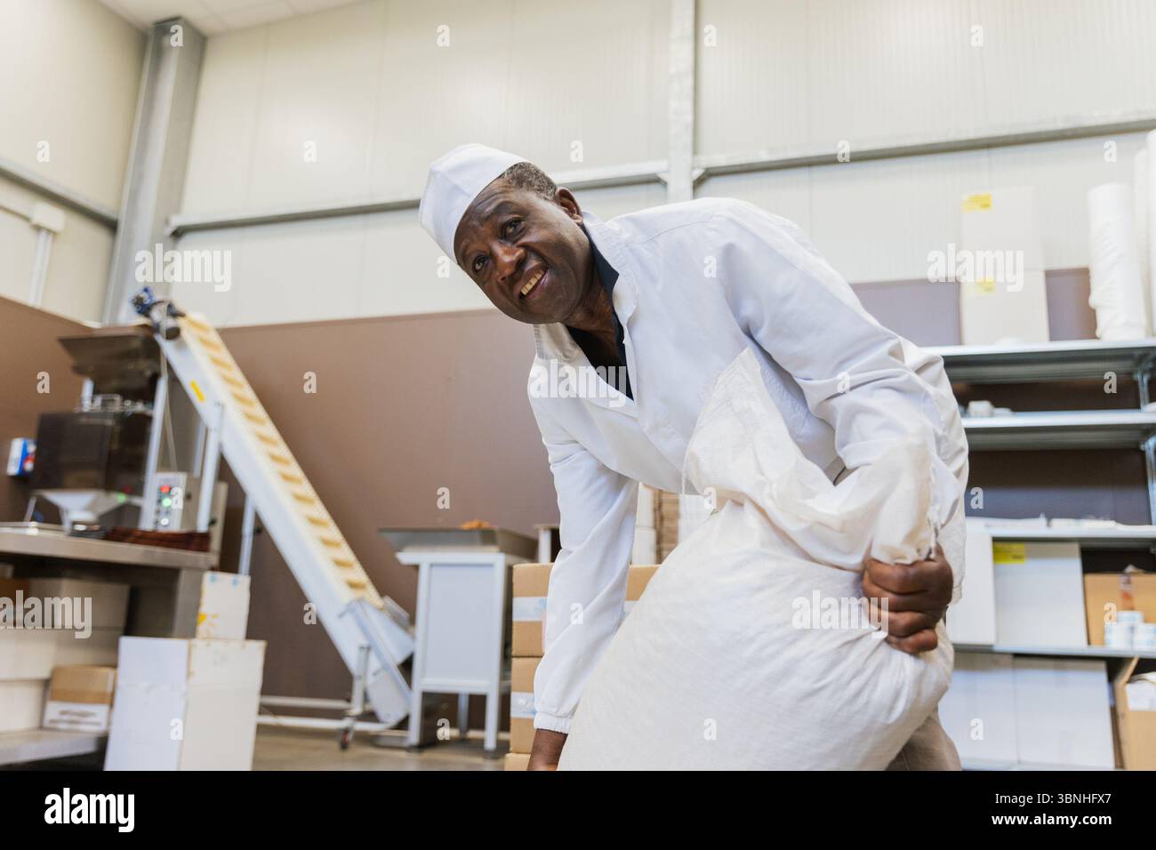 A man in a white lab coat is bending over to lift a sack. The scene is ...