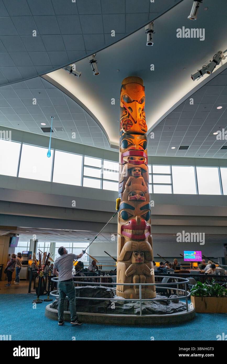 Vancouver, B.C., Canada - June 12, 2025: Vertical photo of worker dusting off a totem pole at ...