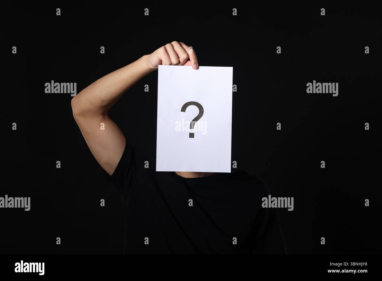 Man hiding behind paper sheet with question mark on dark background ...