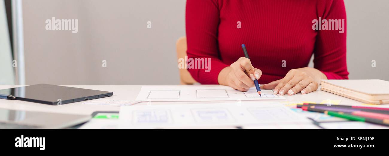 Adult Asian woman uses pencil to sketch user interface designs on paper ...