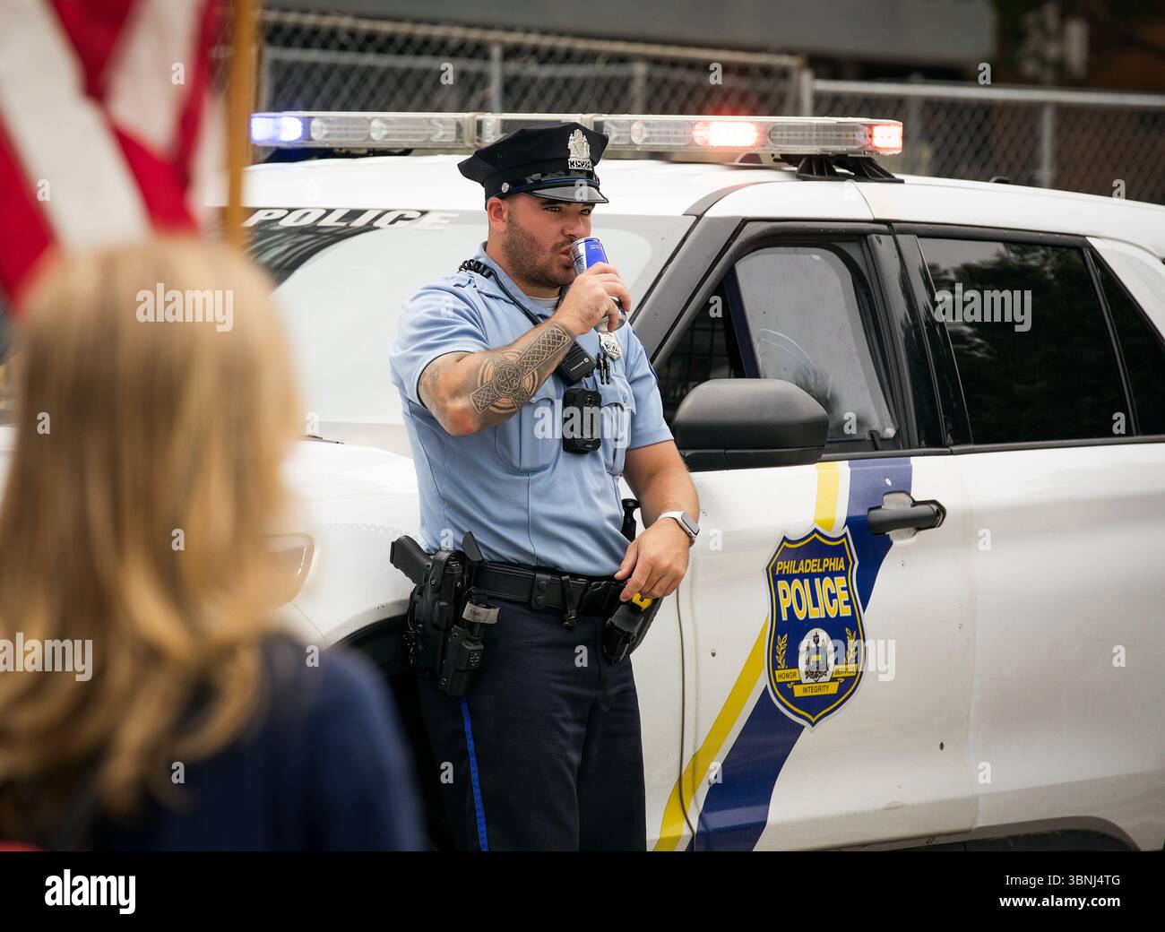 A Philadelphia PD police officer in front of a squad car in ...