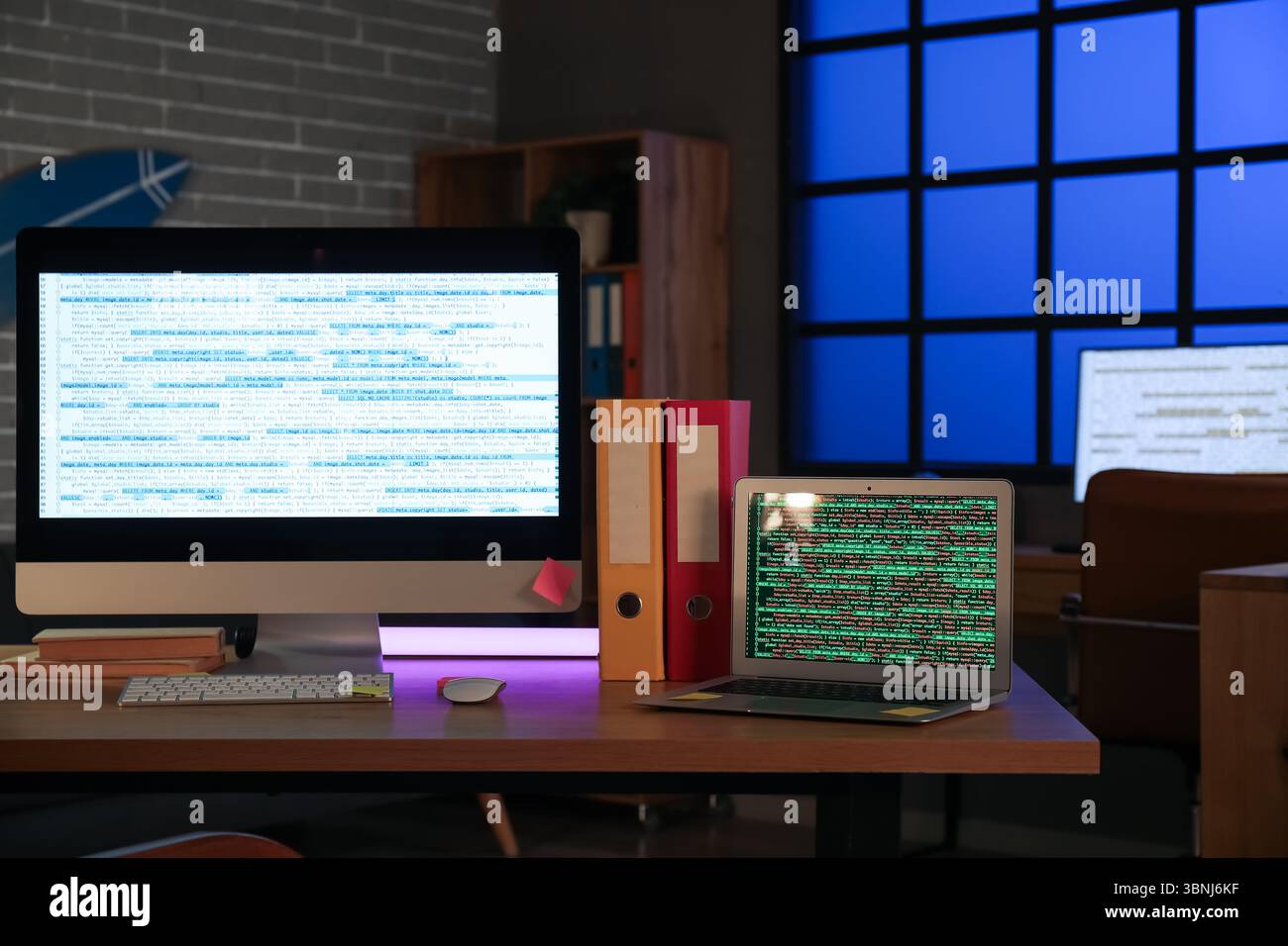 Computer monitor and laptop with codes on programmer's desk in dark ...