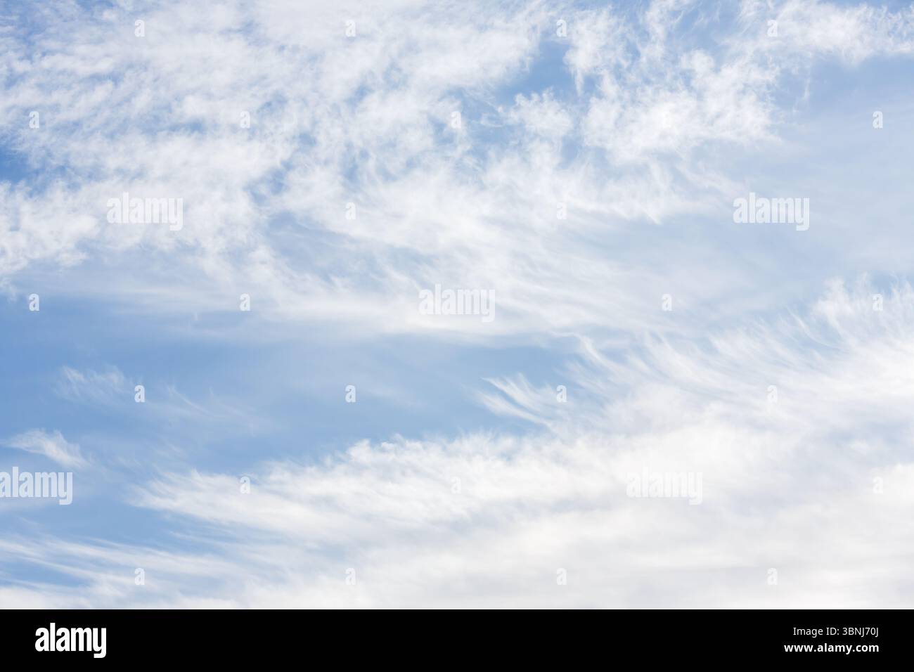Delicate cirrus clouds stretch thinly across a bright blue sky ...