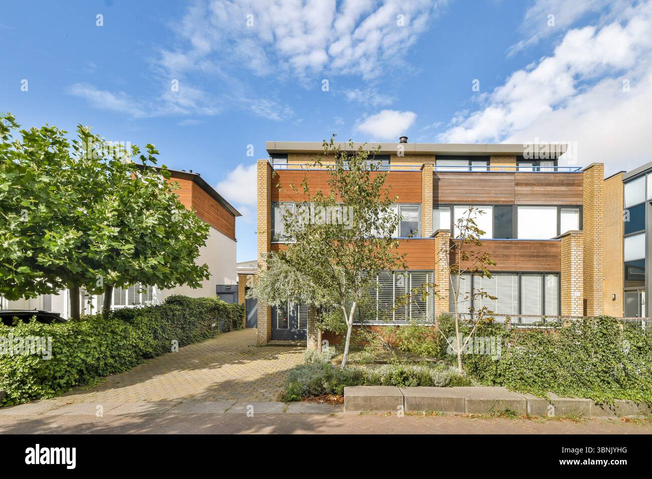 Contemporary suburban home showcasing a stylish facade with wood and brick elements, surrounded ...