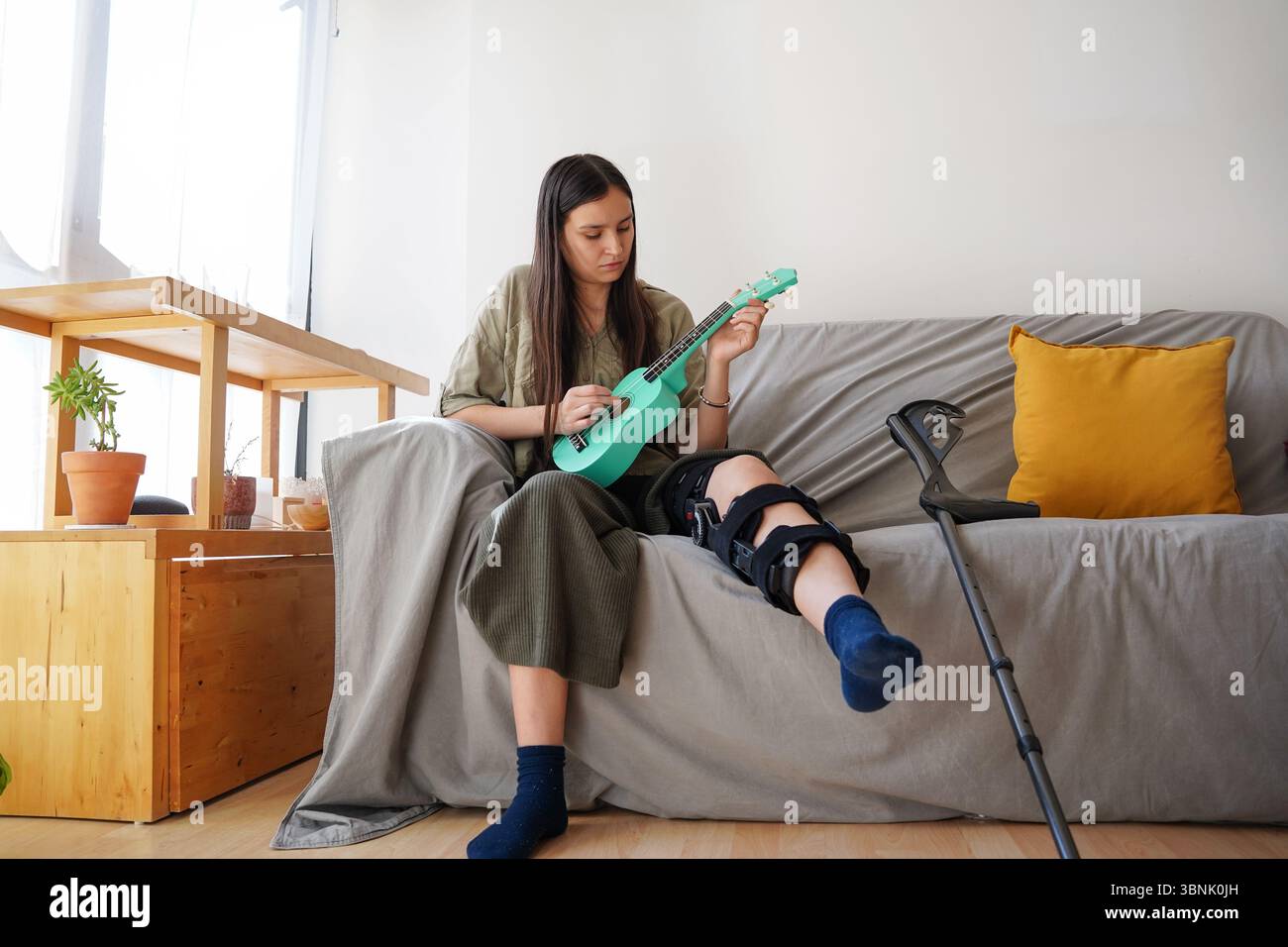 A teen girl with a broken leg, wearing a knee brace, plays a ukulele ...