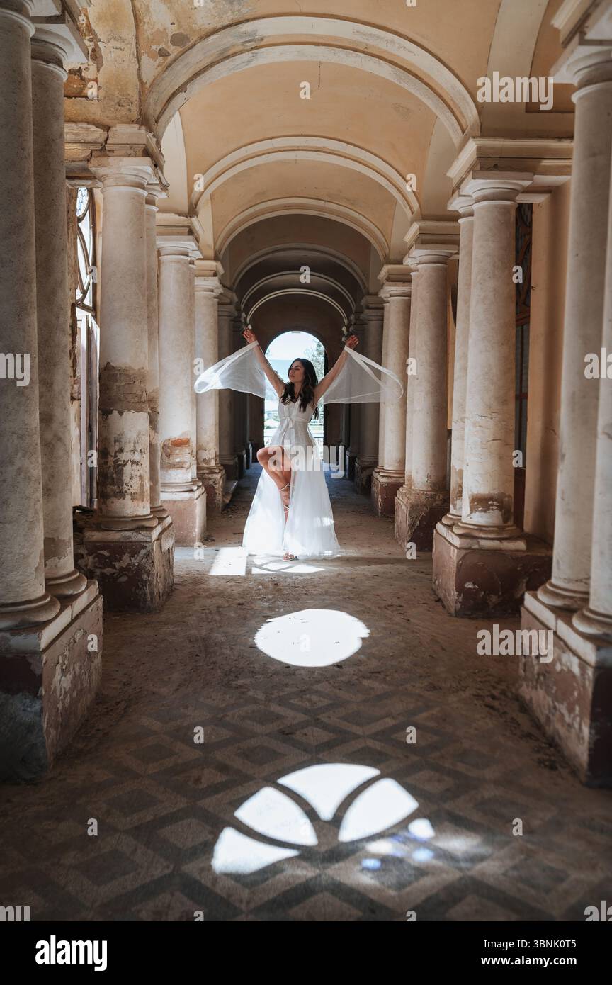 A bride in a flowing white dress poses gracefully in a historic stone ...