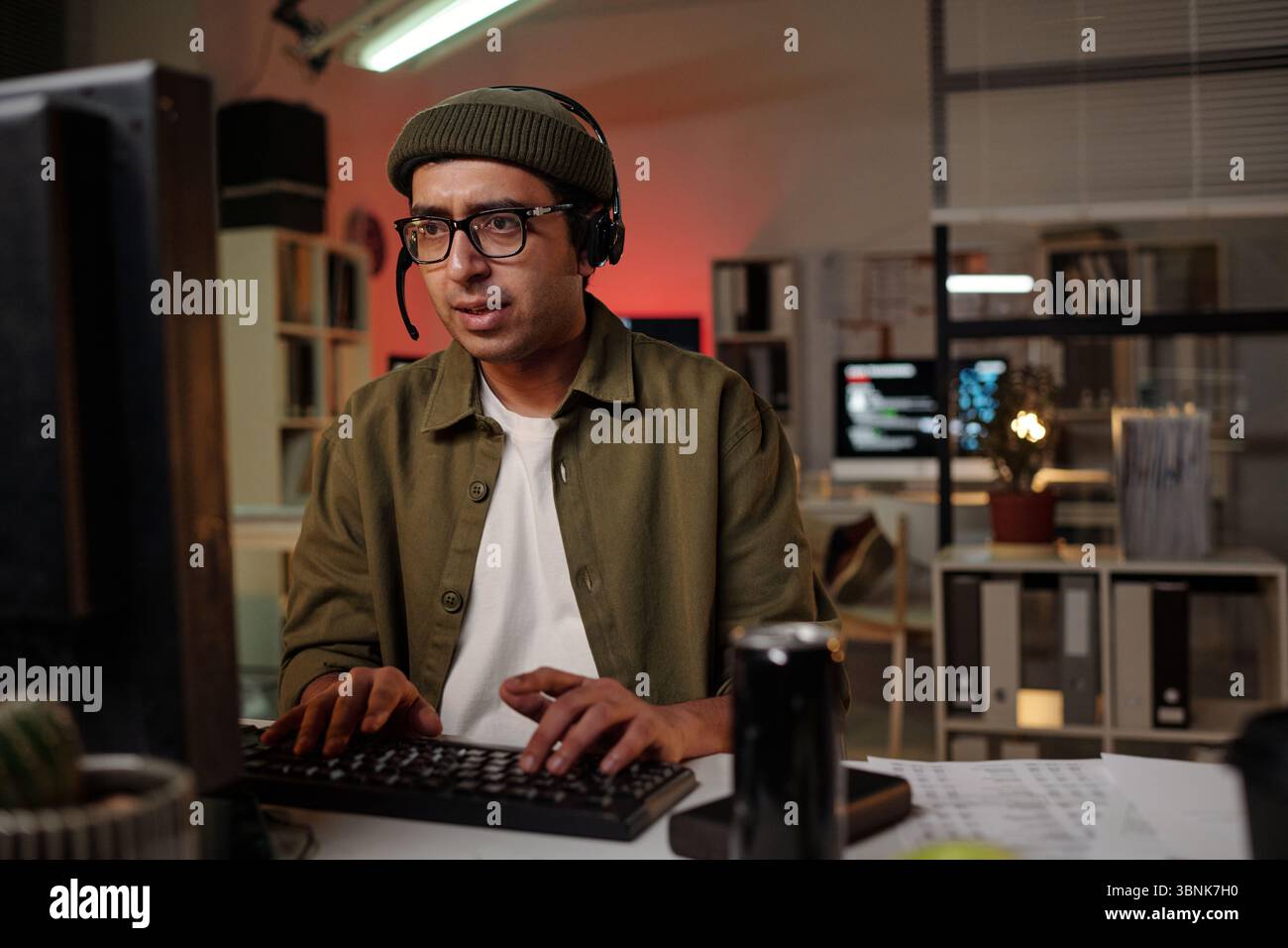South Asian man wearing headset operating computer in office setting ...