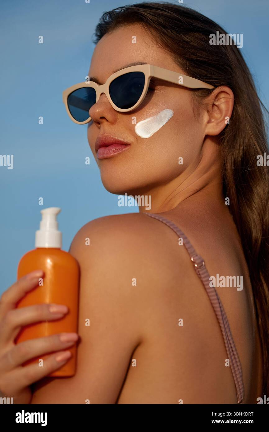 Close-up of a woman applying sunscreen outdoors. She holds a lotion ...