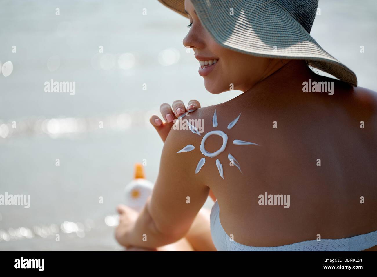 Sunscreen on tanned shoulder. Sun protection. Beautiful woman in bikini applying solar cream ...