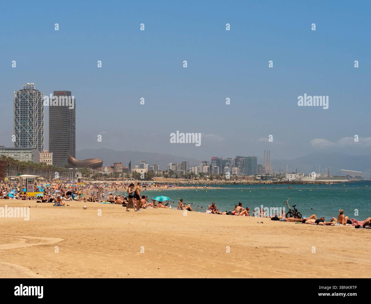 People relaxing on the sand at the popular Barceloneta Beach, with the ...