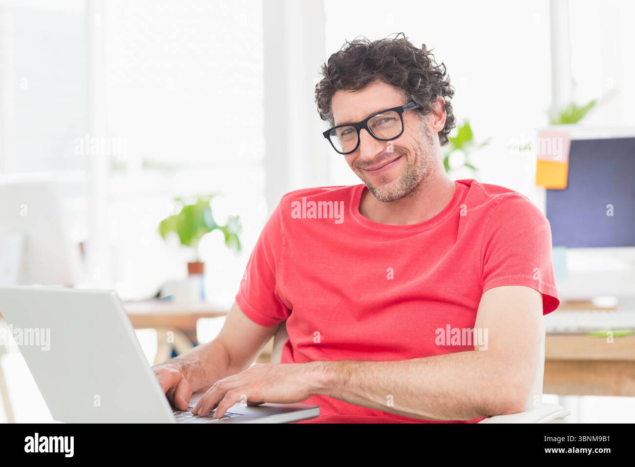 Man typing on laptop at bright office desk, showing sticky notes and ...