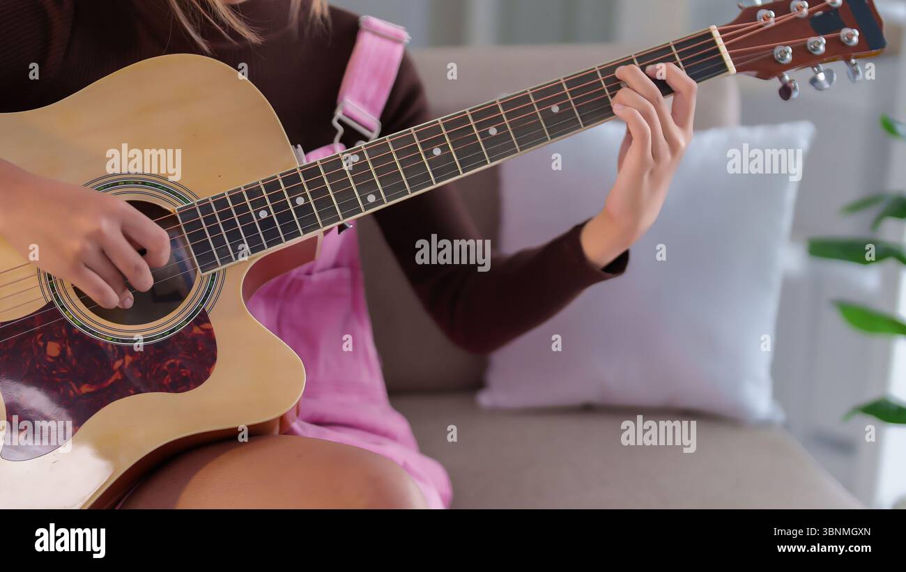 A young Asian woman plays acoustic guitar focusing on hand position on ...