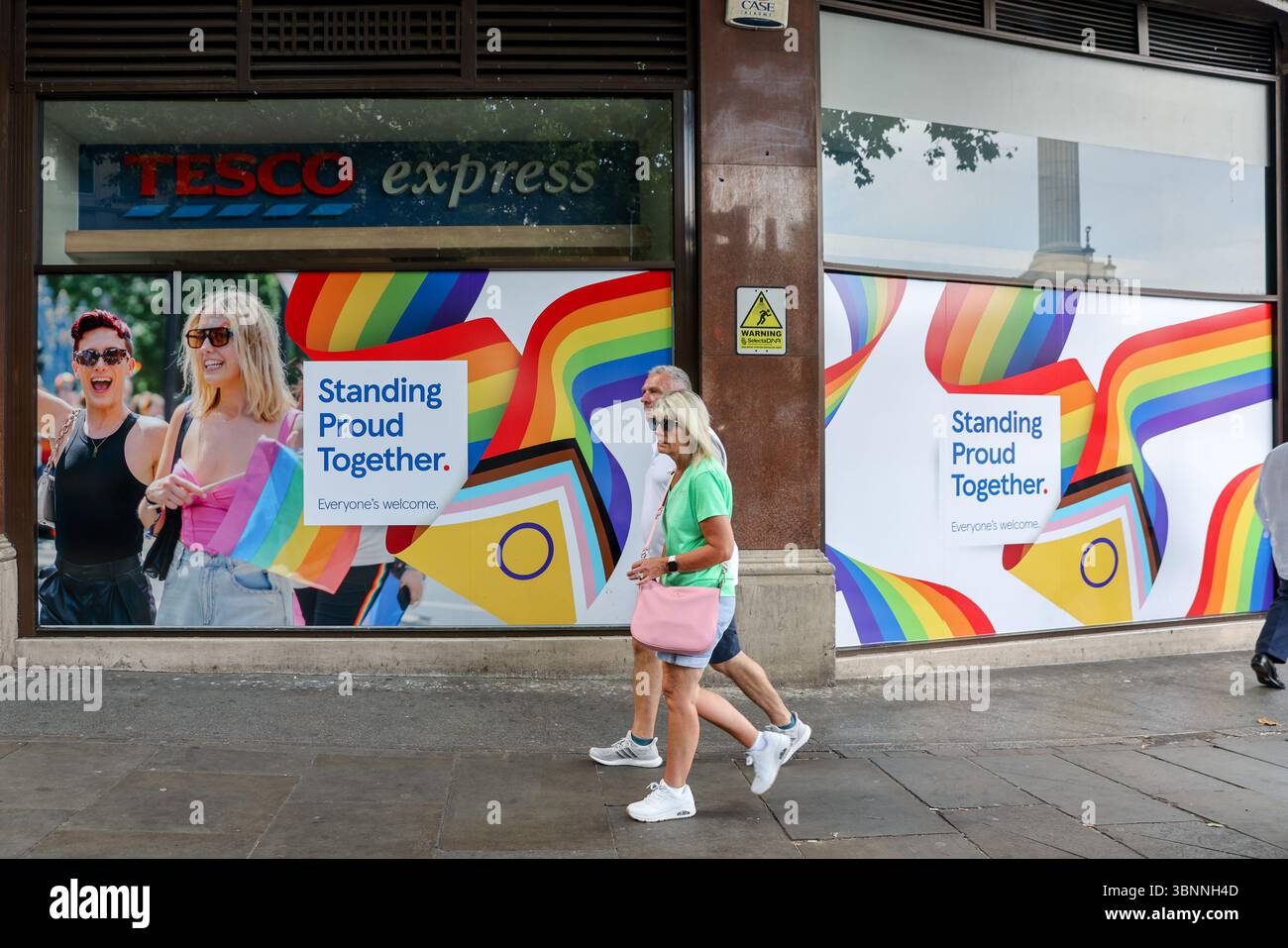 A couple walks past rainbow - colored window decorations at the Tesco ...