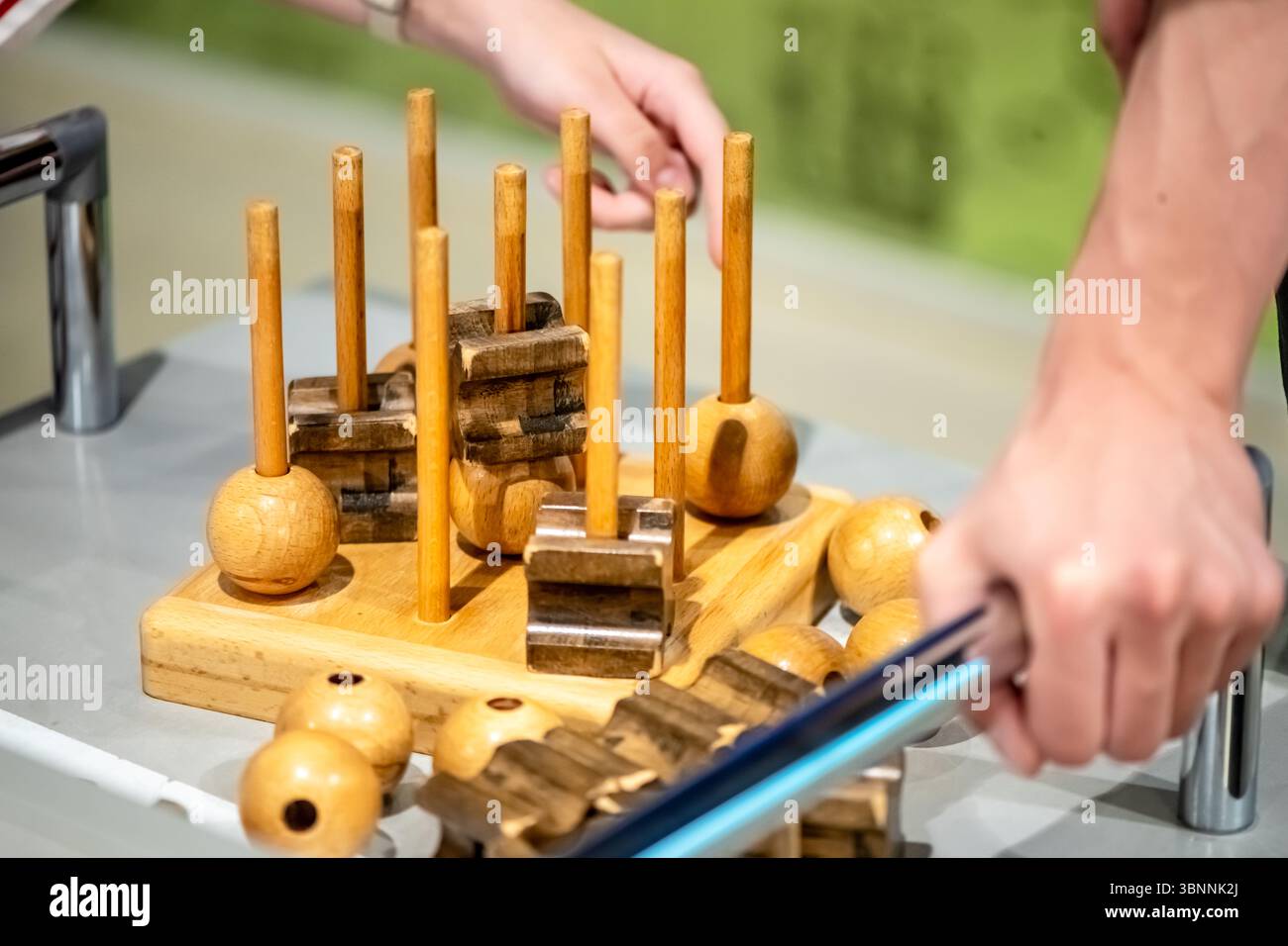 Hands interacting with a wooden puzzle game featuring rods and blocks ...