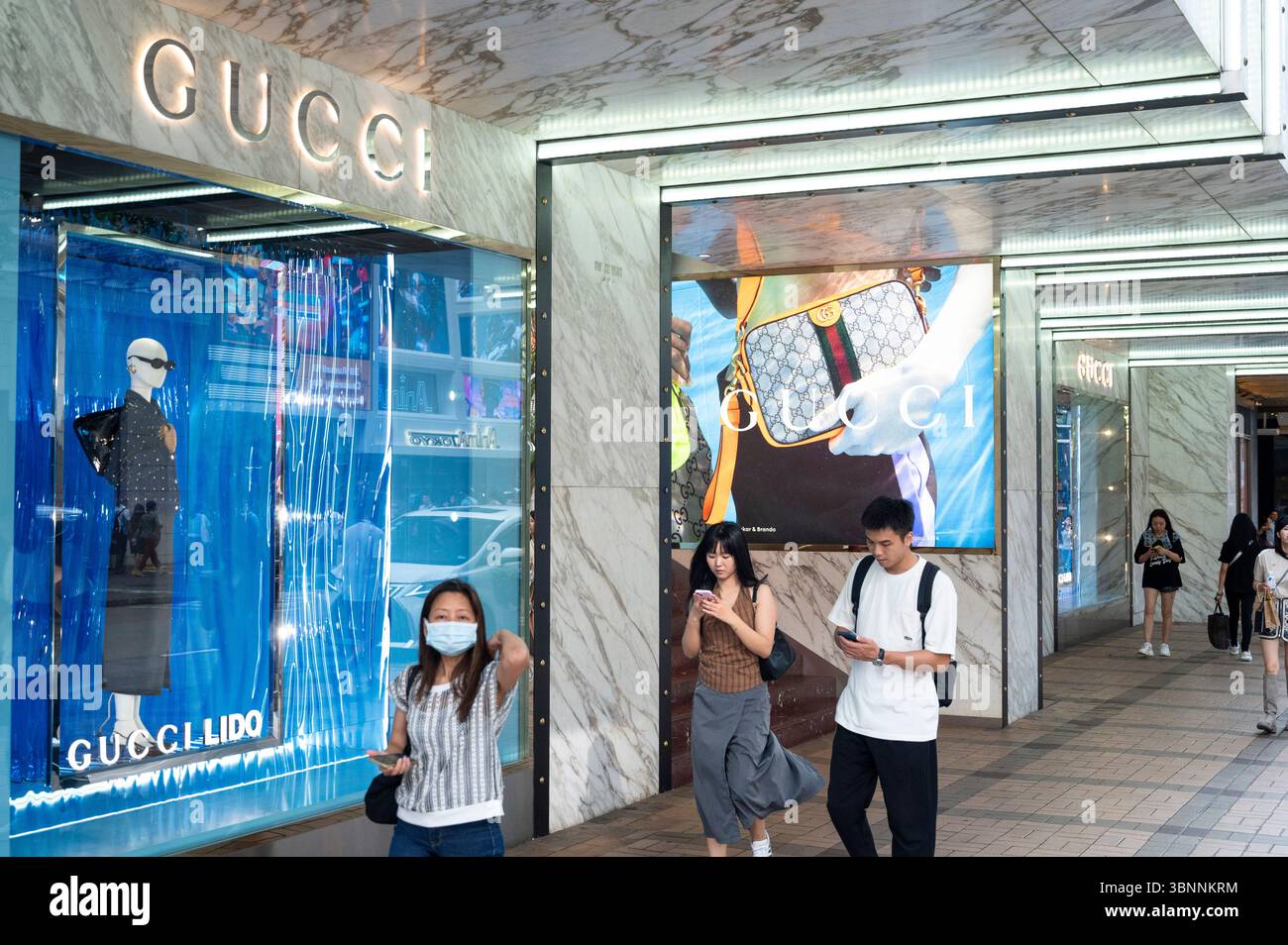 Shoppers walk past the Italian luxury fashion brand Gucci logo and ...