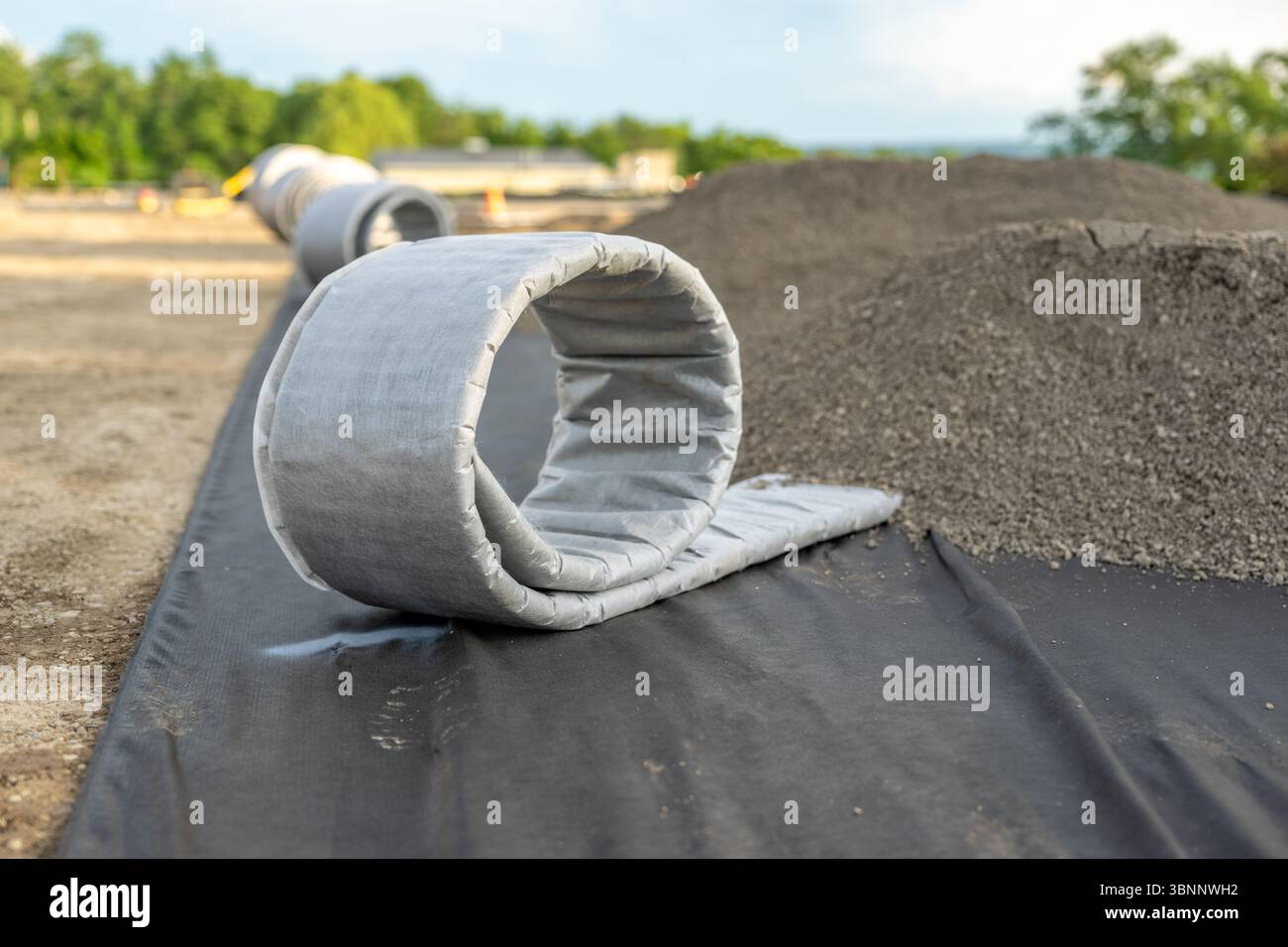 Construction photo of a roll of flat panel drainage pipe being installed on a synthetic turf ...
