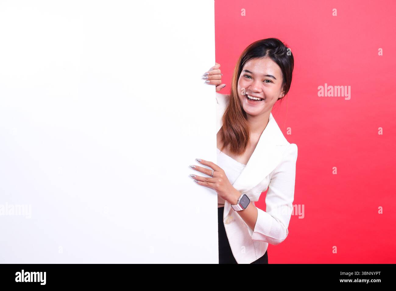 A smiling woman peeking behind a large blank white sign, she is wearing ...