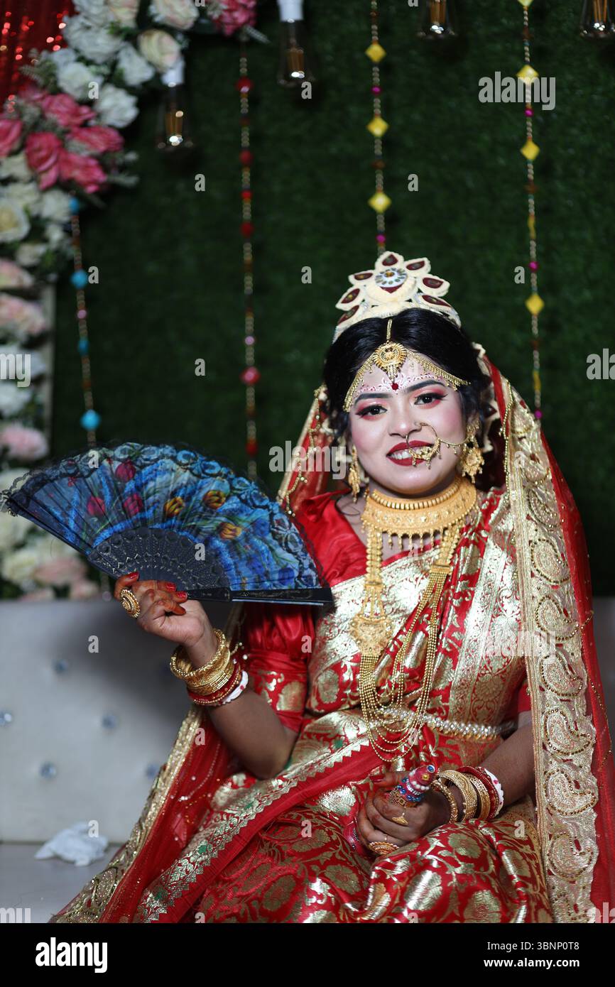 Beautiful bengali bride in traditional red and gold attire holding a ...