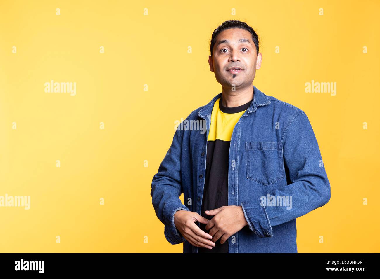Portrait of cheerful confident indian man smiling standing against orange background, looking ...