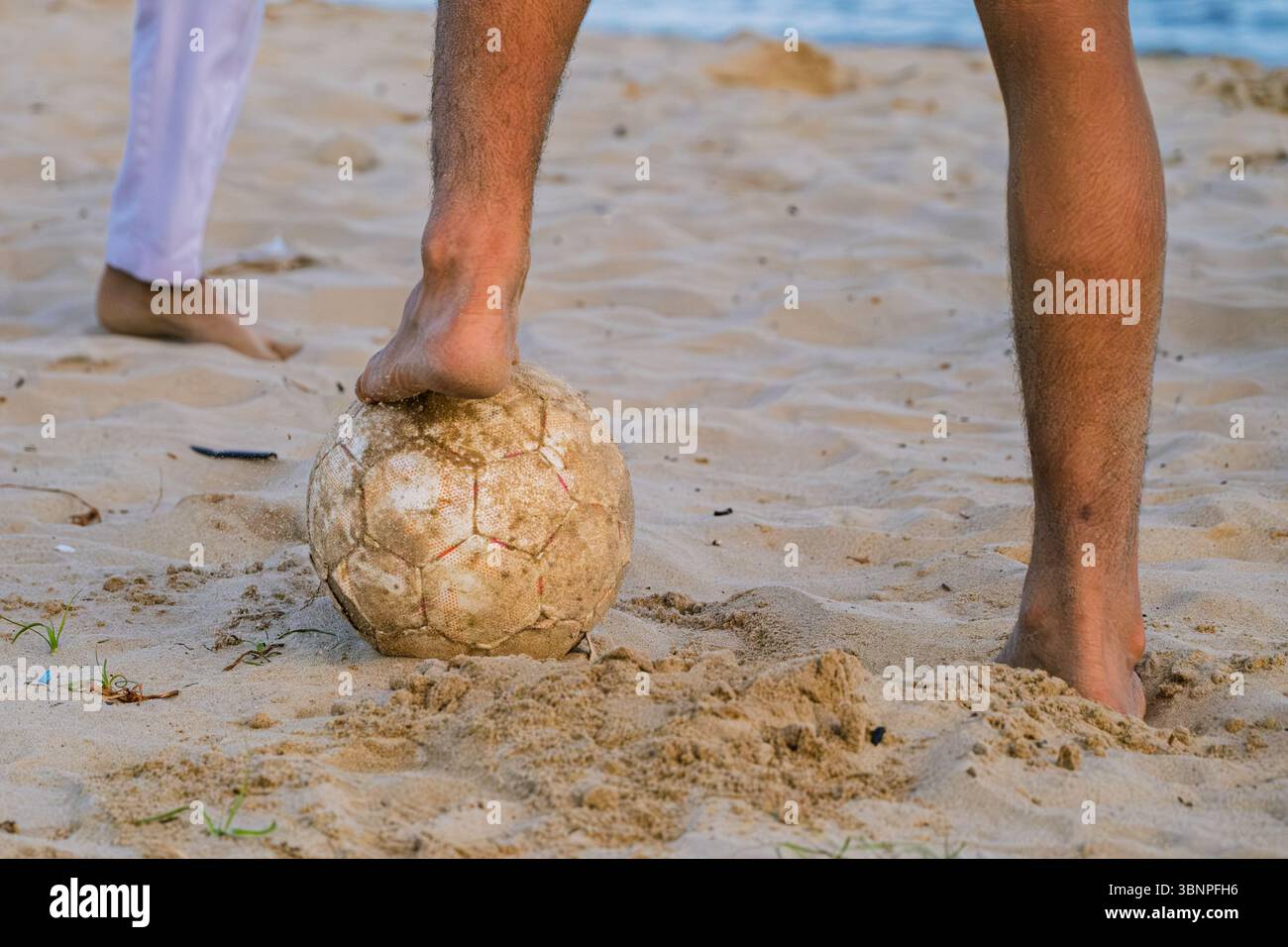 Close-up of a barefoot player’s foot resting on a worn-out soccer ball ...