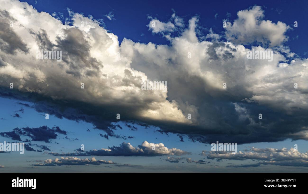 Vast clouds gather and disperse in a vibrant blue sky, creating ...