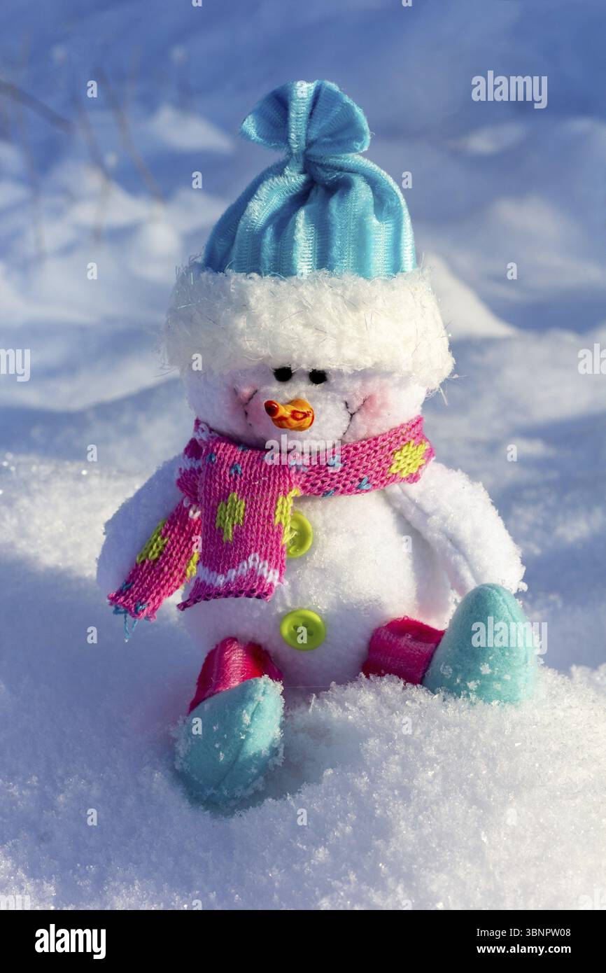 New year Christmas toy snowman in a blue cap sitting on the snow in a ...