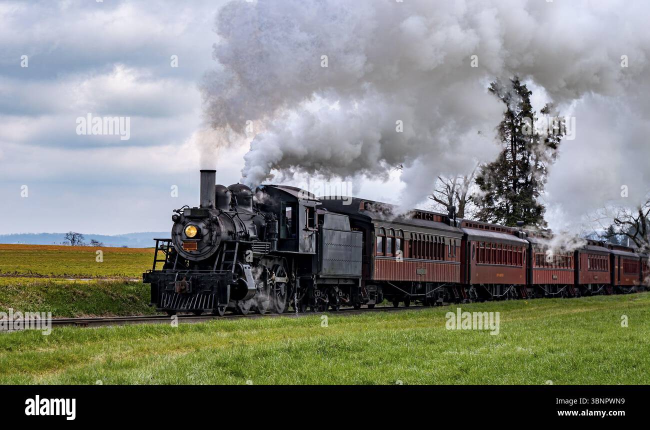 A vintage steam locomotive chugs along a railway line, billowing white ...