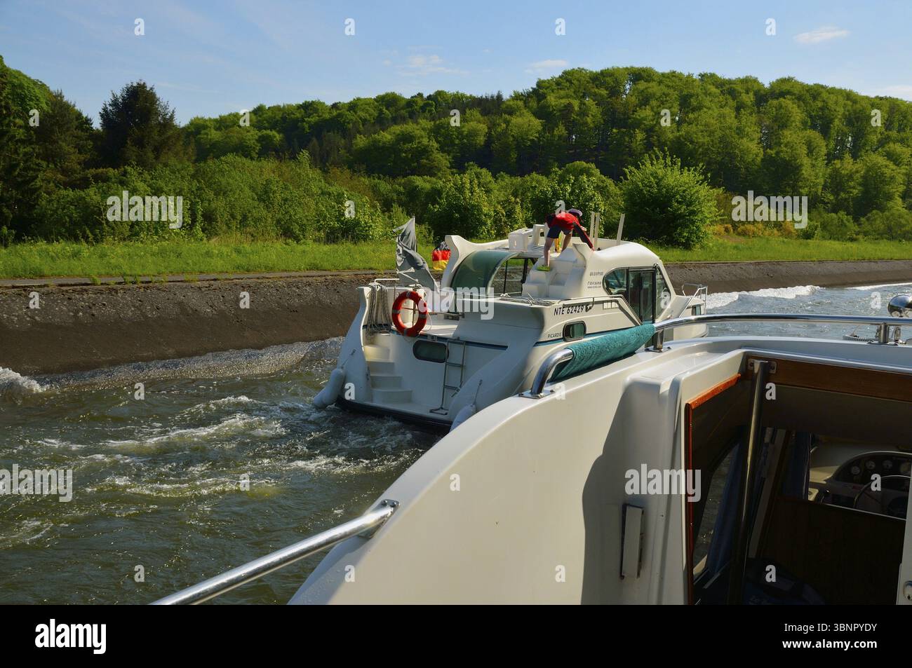 Two boats sailing on a river, surrounded by green trees and blue sky ...